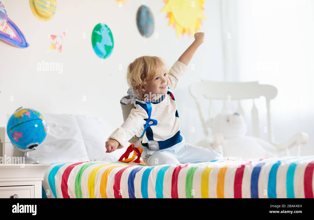 Kids play astronaut. Little boy in space costume jumping on bed with ...