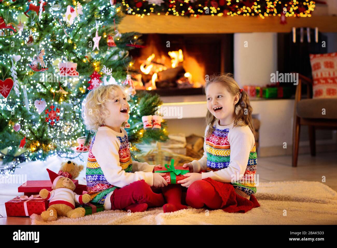 Children at Christmas tree and fireplace on Xmas eve. Family with kids ...
