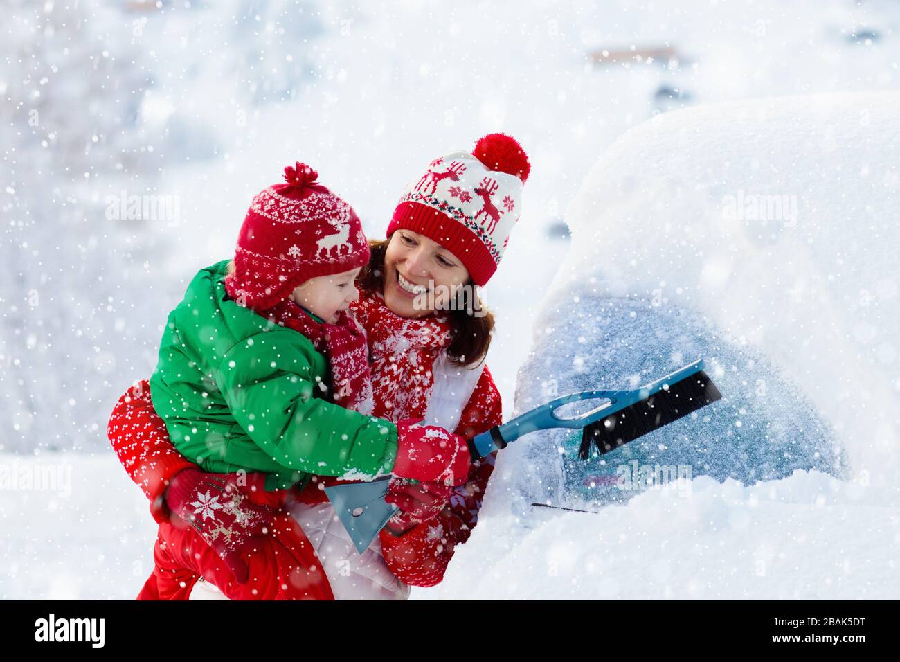 Mother and child brushing and shoveling snow off car after storm ...