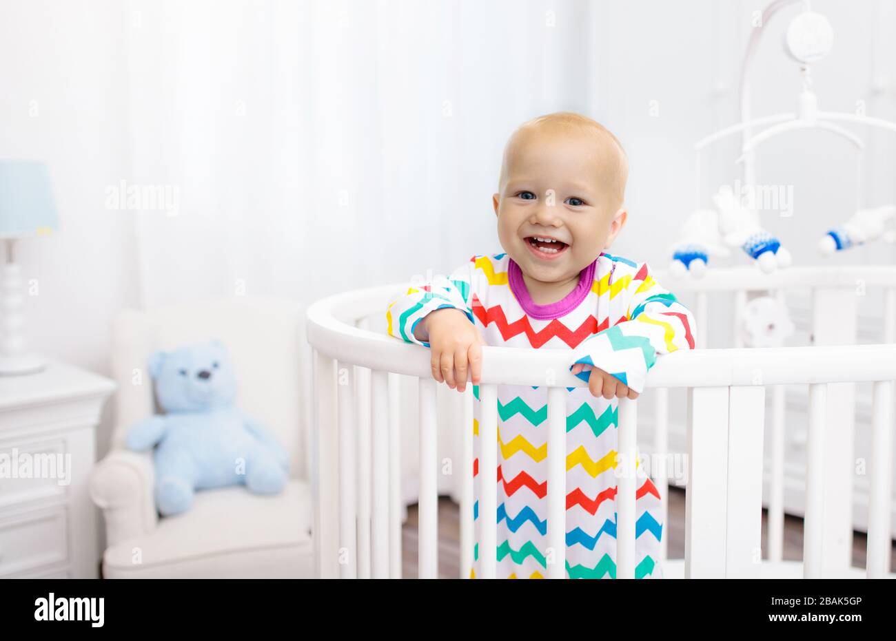 Cute laughing baby standing in bed after nap time. Nursery interior for ...