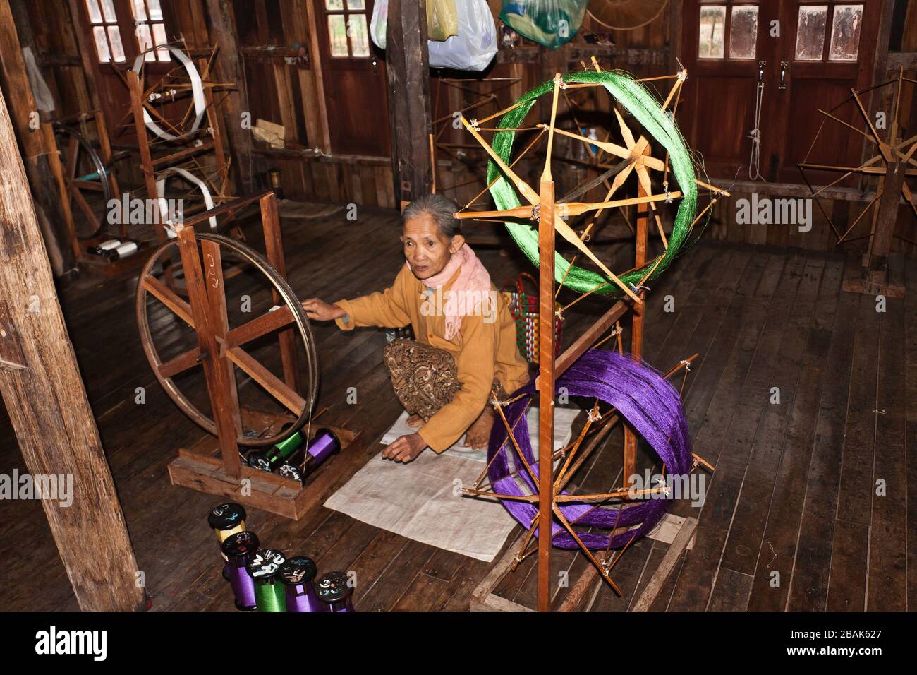A senior Burmese woman working at a vintage hand loom in a village ...