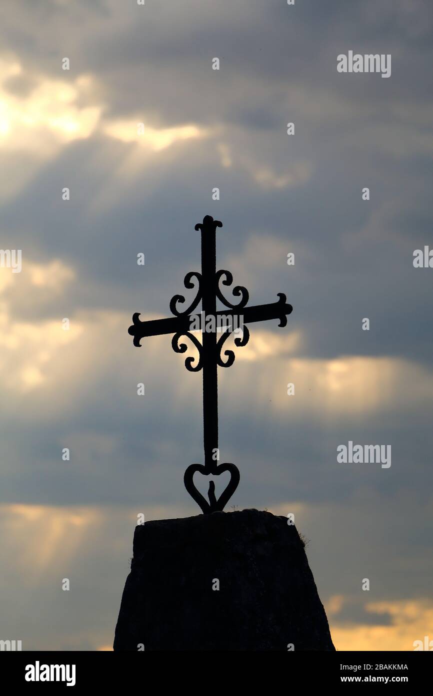 A very old black christian cross with a cloudy sky in background ...