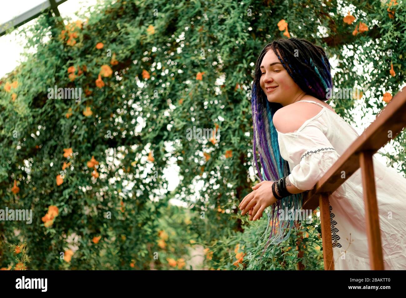 Lovely girl with multi-colored dreadlocks in a white dress stands on a ...