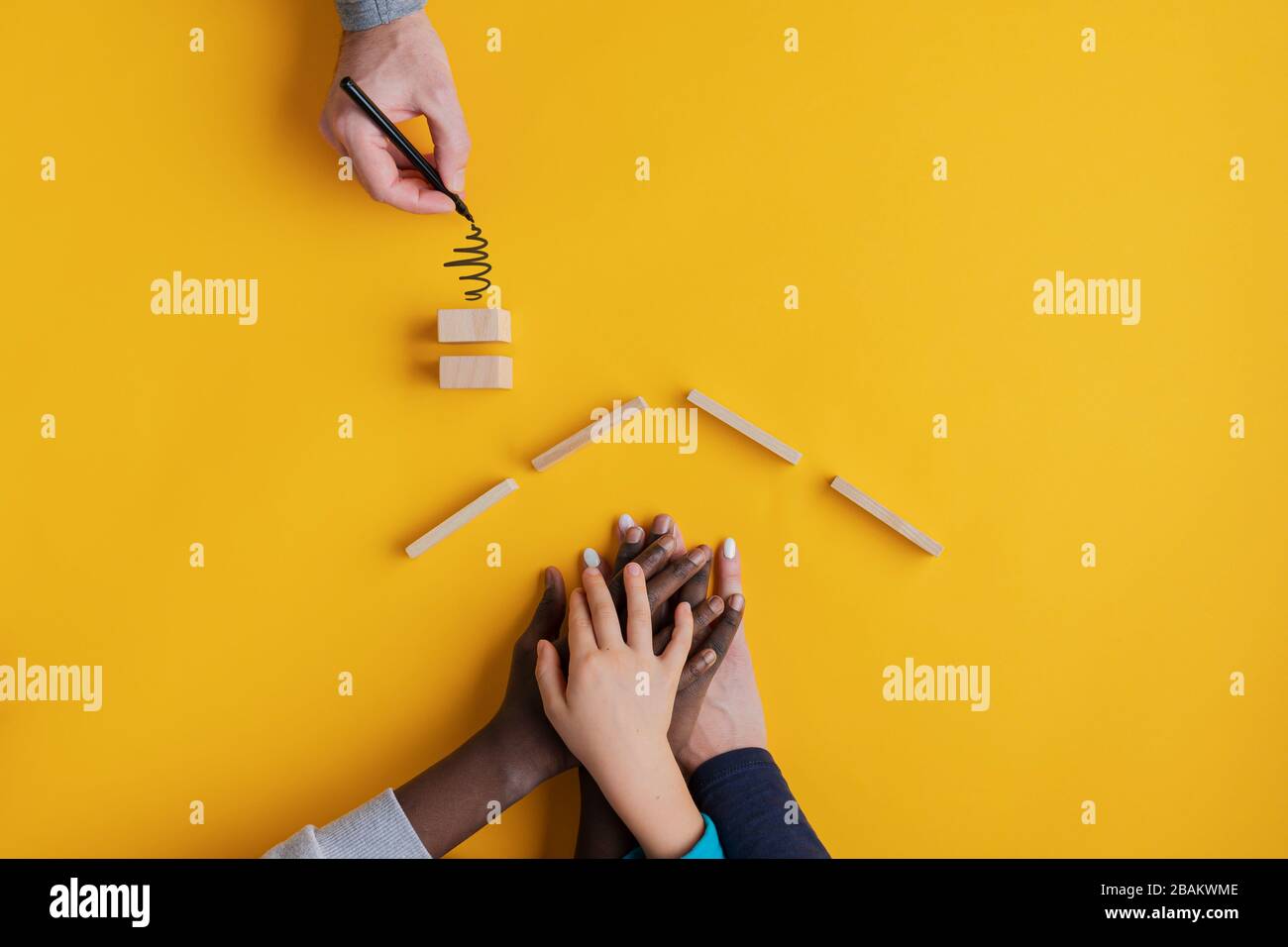 Hand of a father making a house build of wooden blocks for his mixed ...