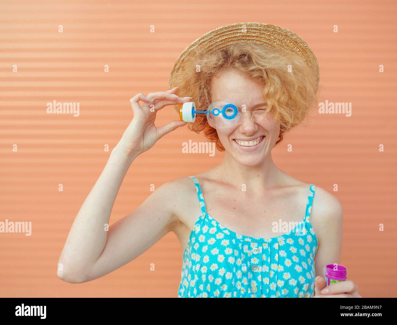 young cheerful curly redhead woman in blue sundress and straw hat with ...
