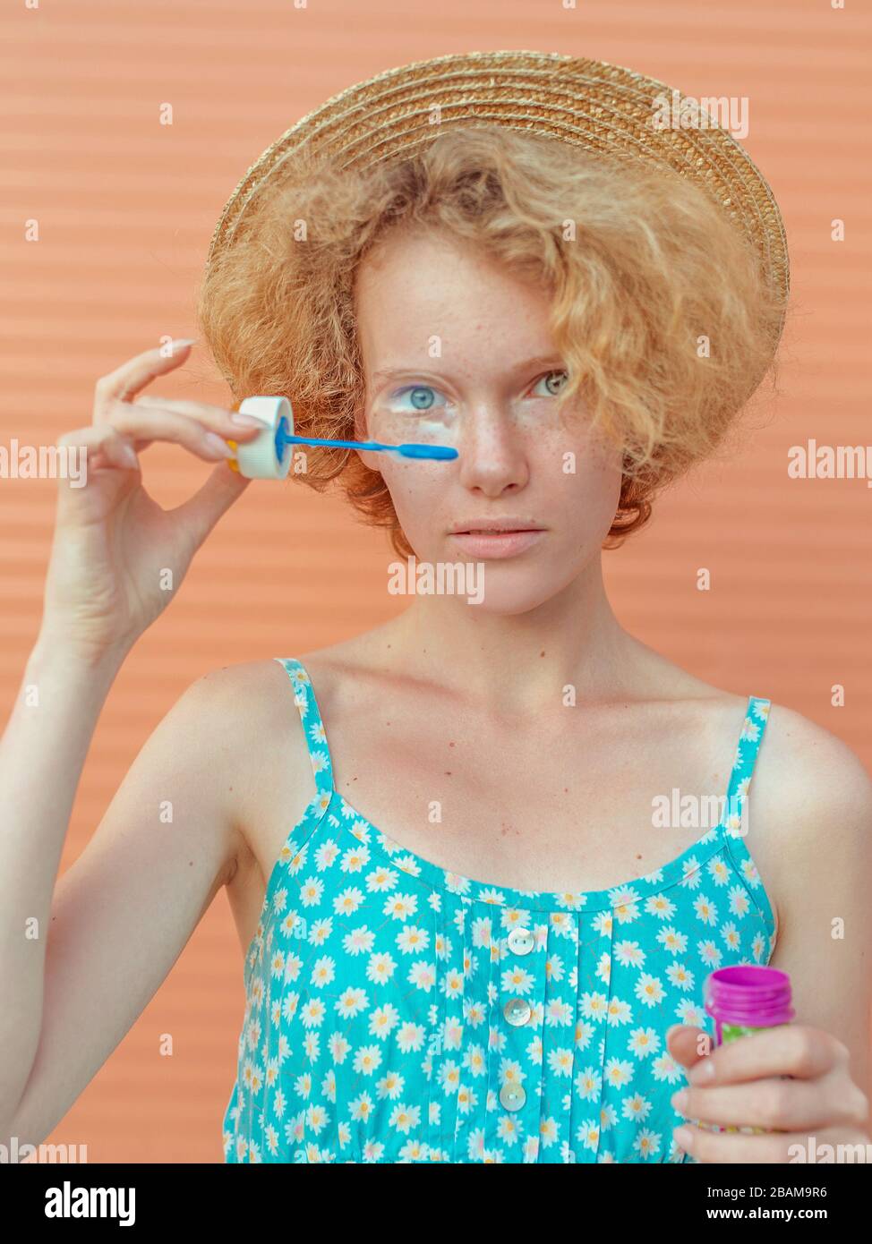 young cheerful curly redhead woman in blue sundress and straw hat with ...
