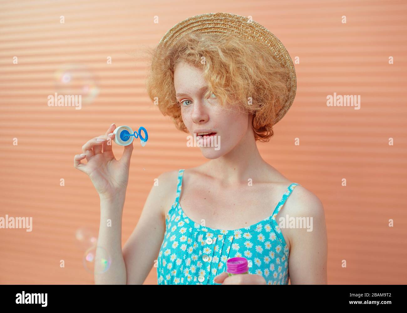 young cheerful curly redhead woman in blue sundress and straw hat with ...