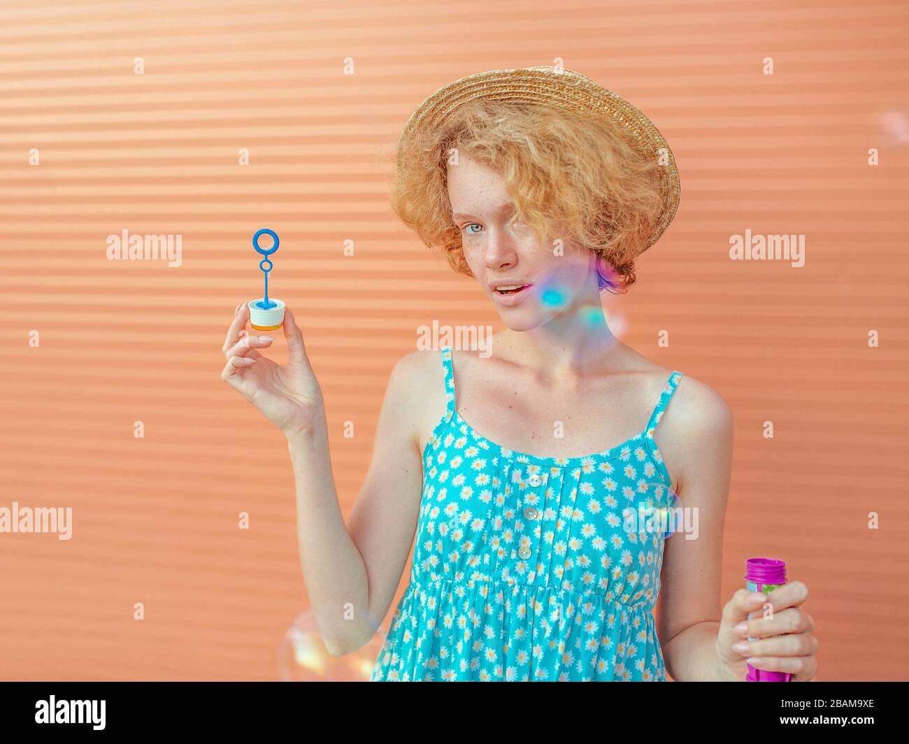 young cheerful curly redhead woman in blue sundress and straw hat with ...