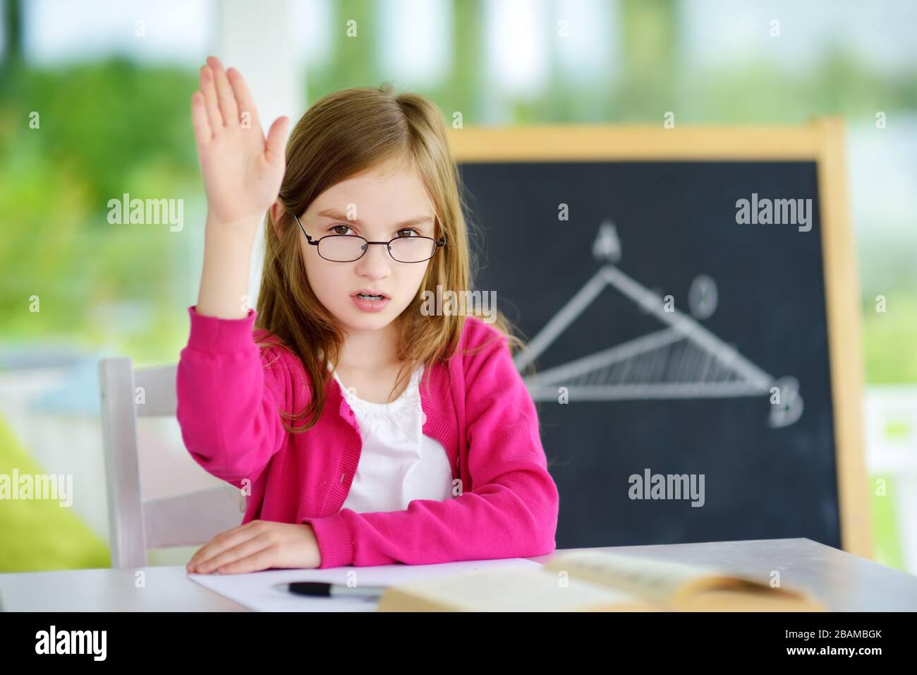 Smart schoolgirl studying with a pile of books on her desk. Young girl ...