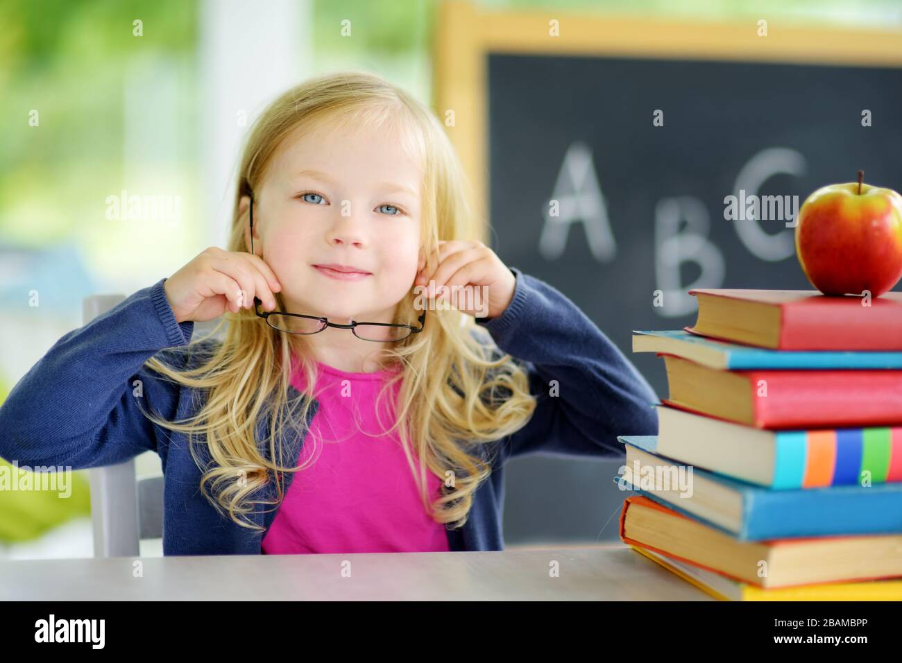 Smart schoolgirl studying with a pile of books on her desk. Young girl ...
