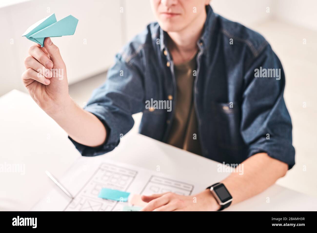Close-up of young man sitting at table and throwing paper plane while ...