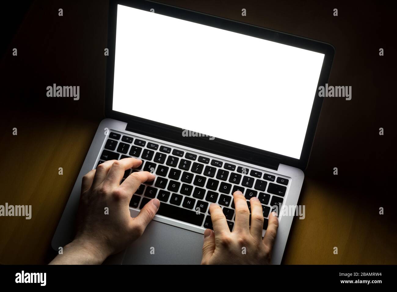 Man working on laptop with white screen glowing in the dark from above ...