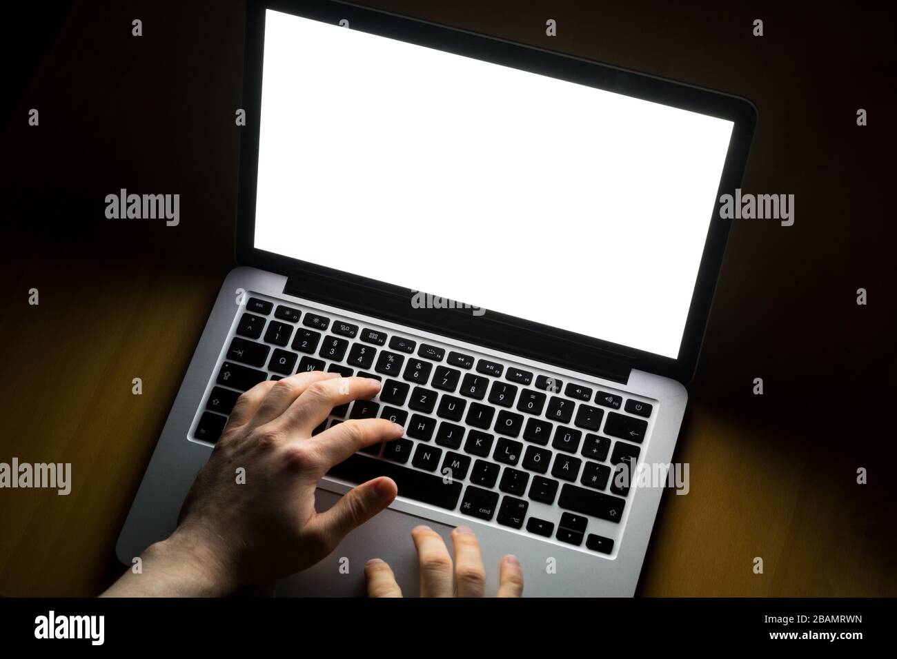 Man working on laptop with white screen glowing in the dark from above ...