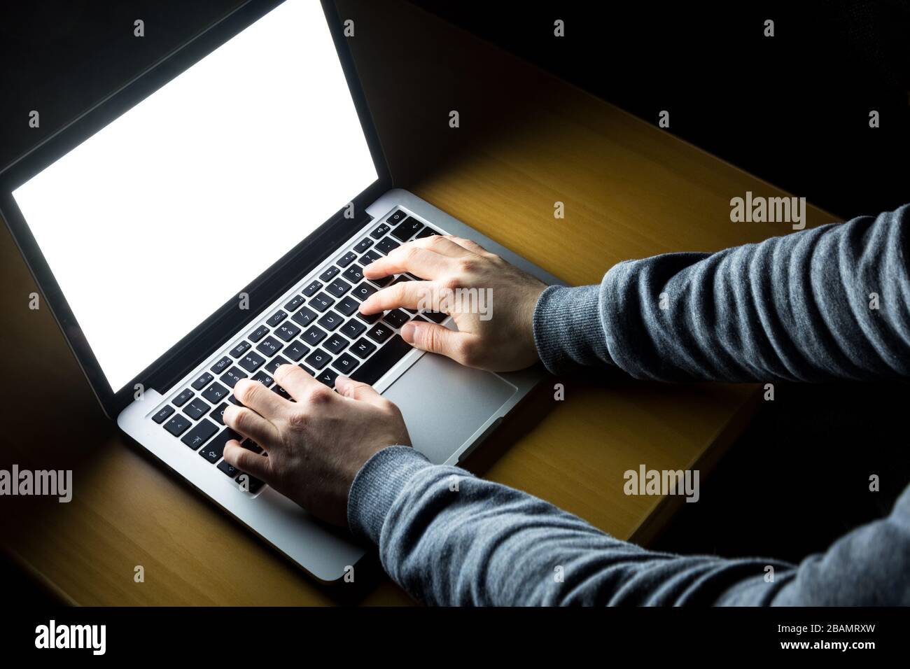 Man working on laptop with white screen glowing in the dark on a wooden ...