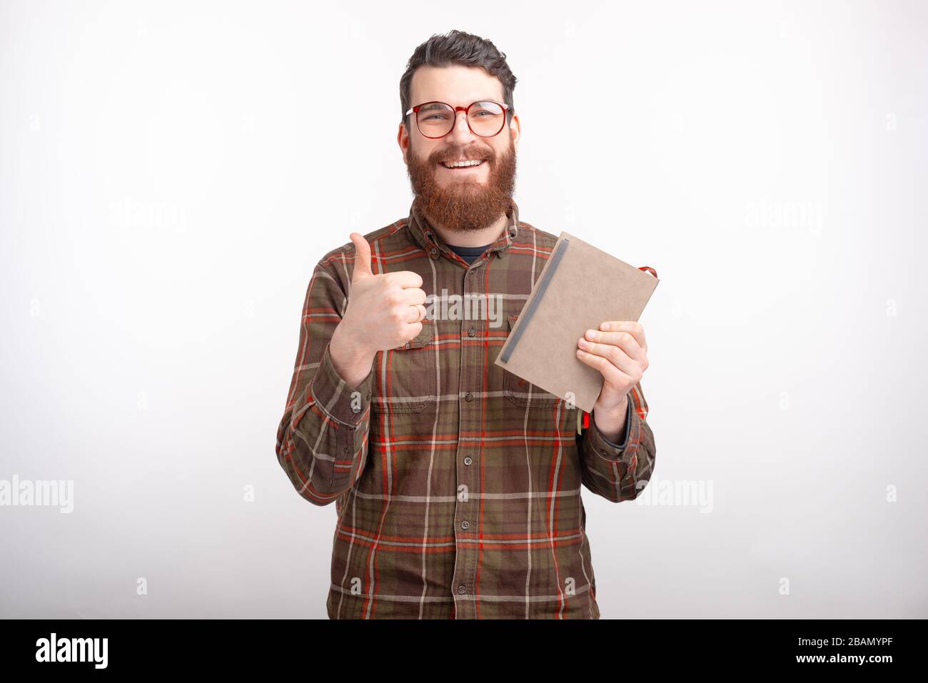 Happy young man is holding a notebook or a book, smiling at the camera ...