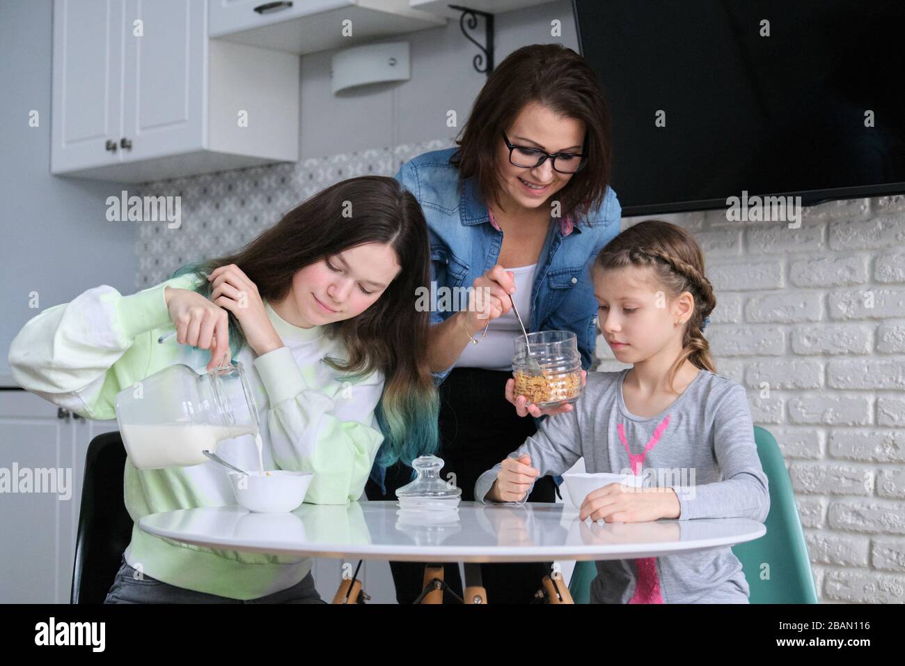 Children with mother eating at home in kitchen, two girls sitting at ...