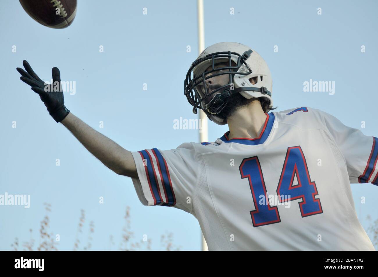 Player jumping to catch American football ball with the sky as ...