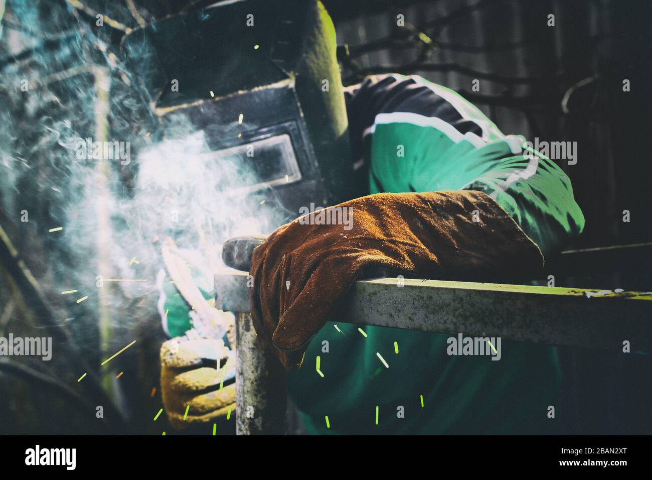 A man in weld mask with electric weld in his hand welding a metal frame ...