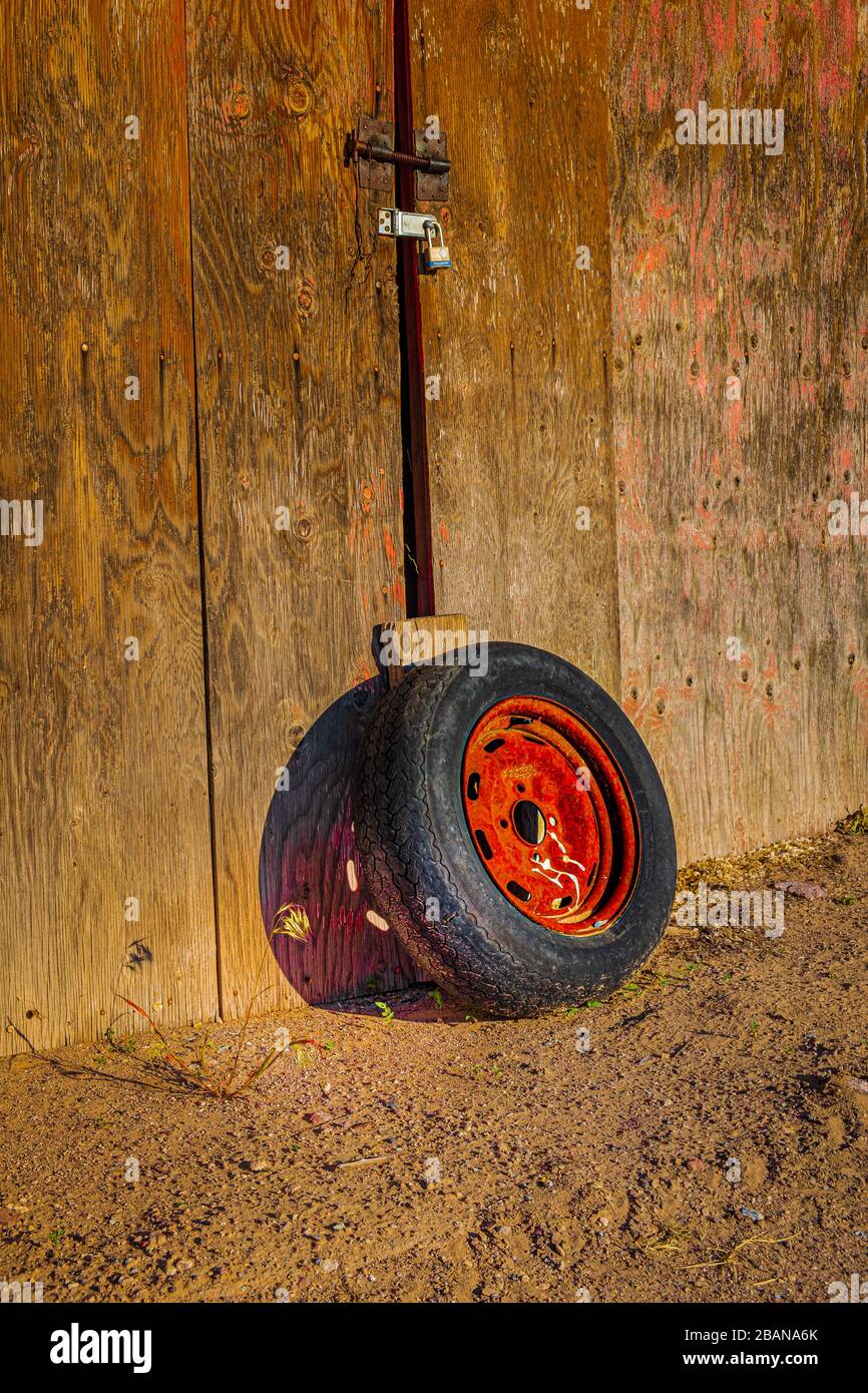 A well-used red-rimmed tire sits agaiinst a shed door as the sun casts ...