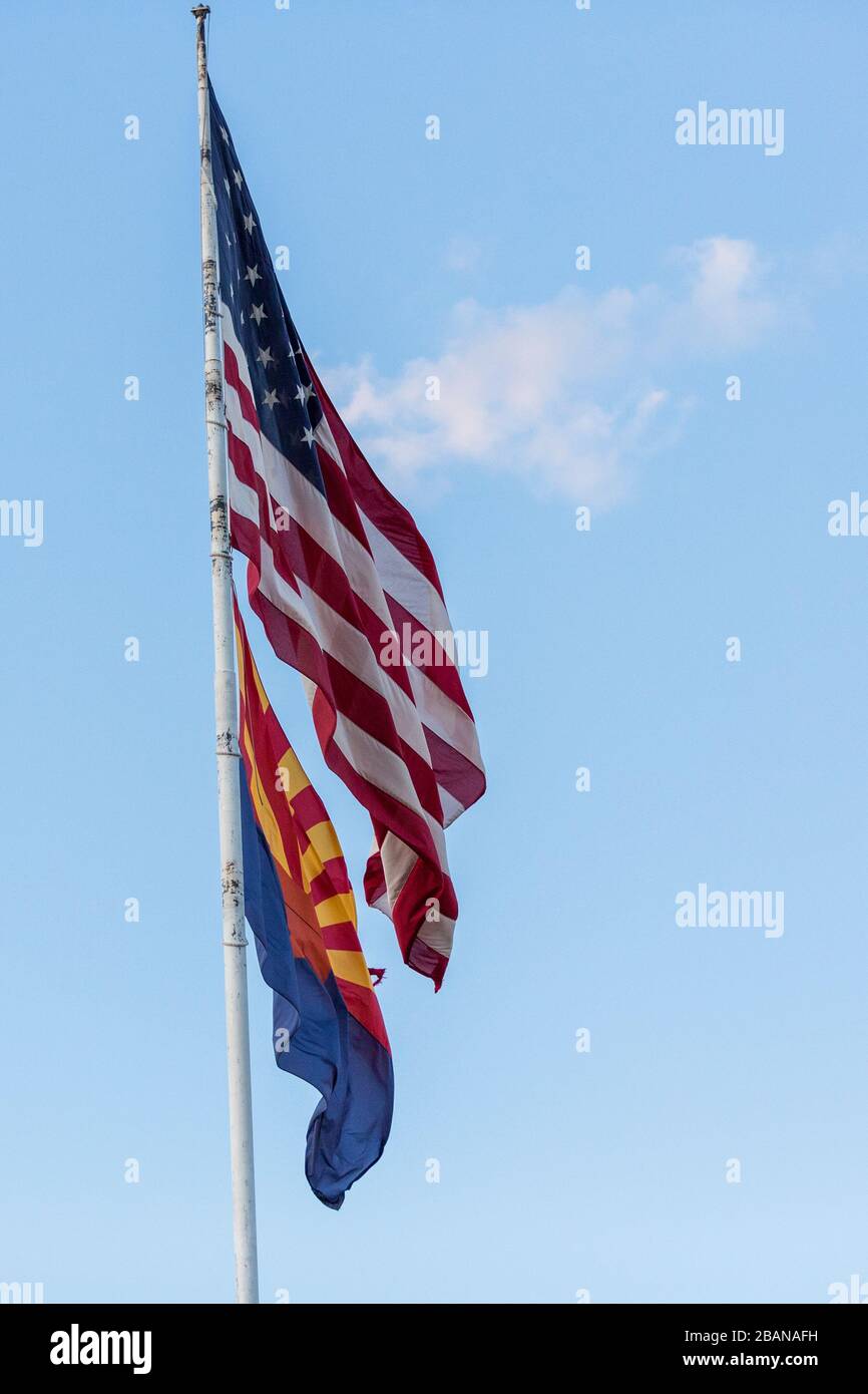 American and arizona state flag flying against a blue sky with light ...
