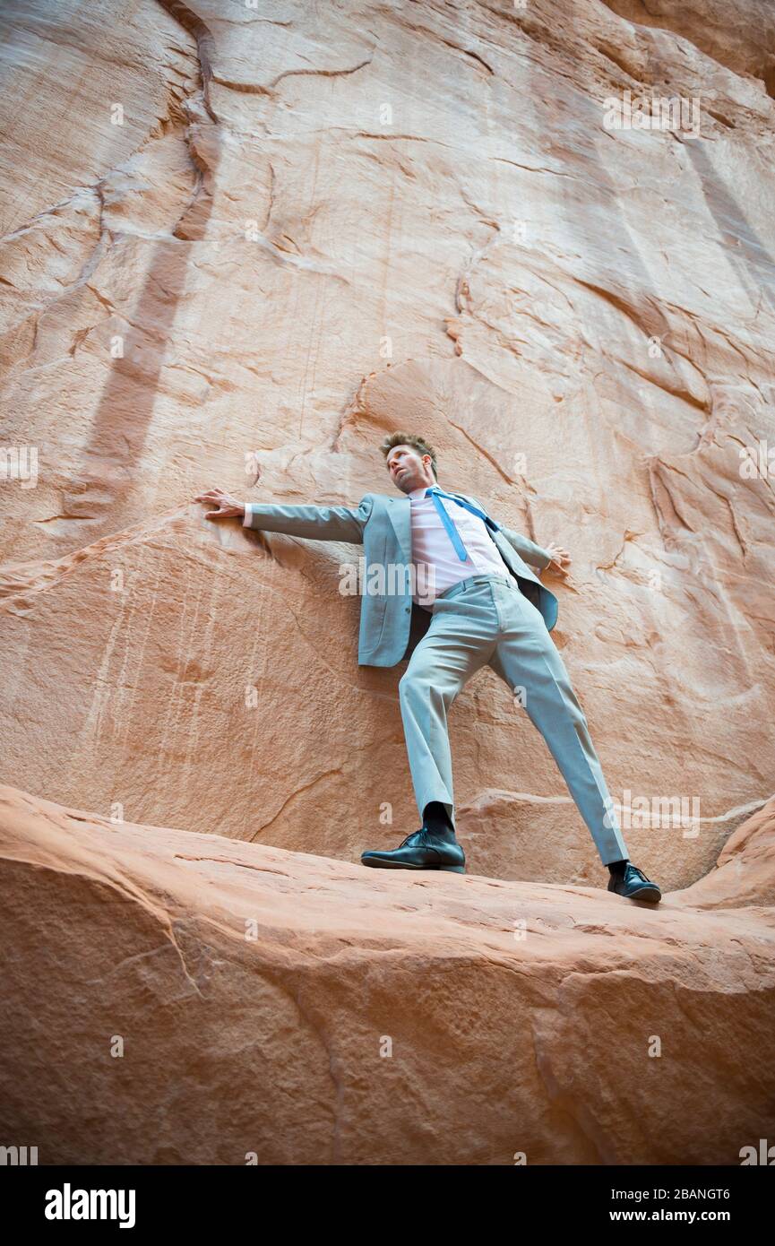 Nervous businessman clinging to a cliff face while balancing on a ...