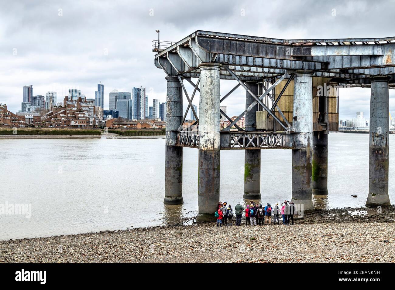 A tour group standing on the Thames riverbank by the old coal jetty of ...