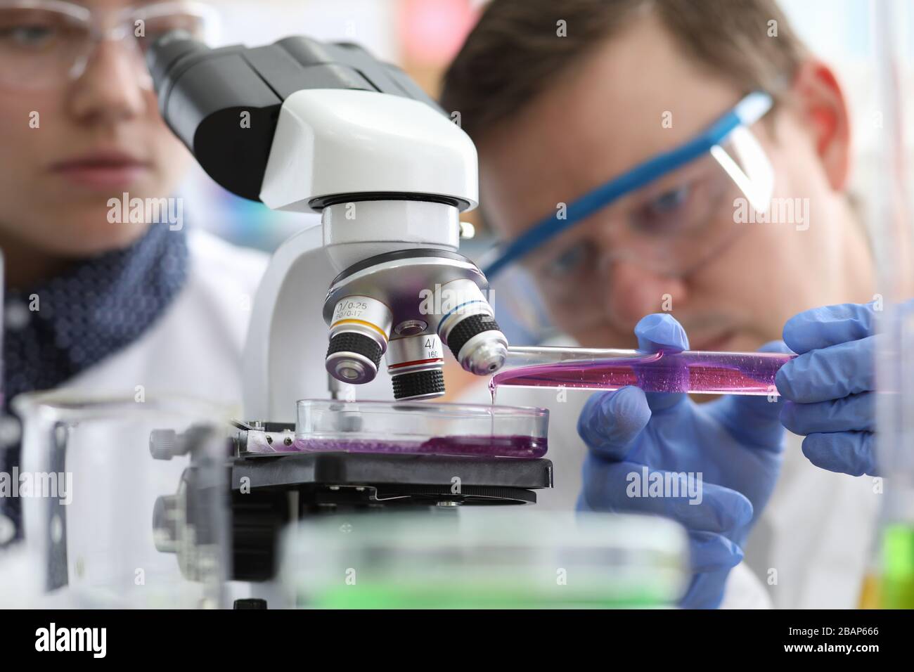 Man pours liquid into test tube under microscope Stock Photo - Alamy