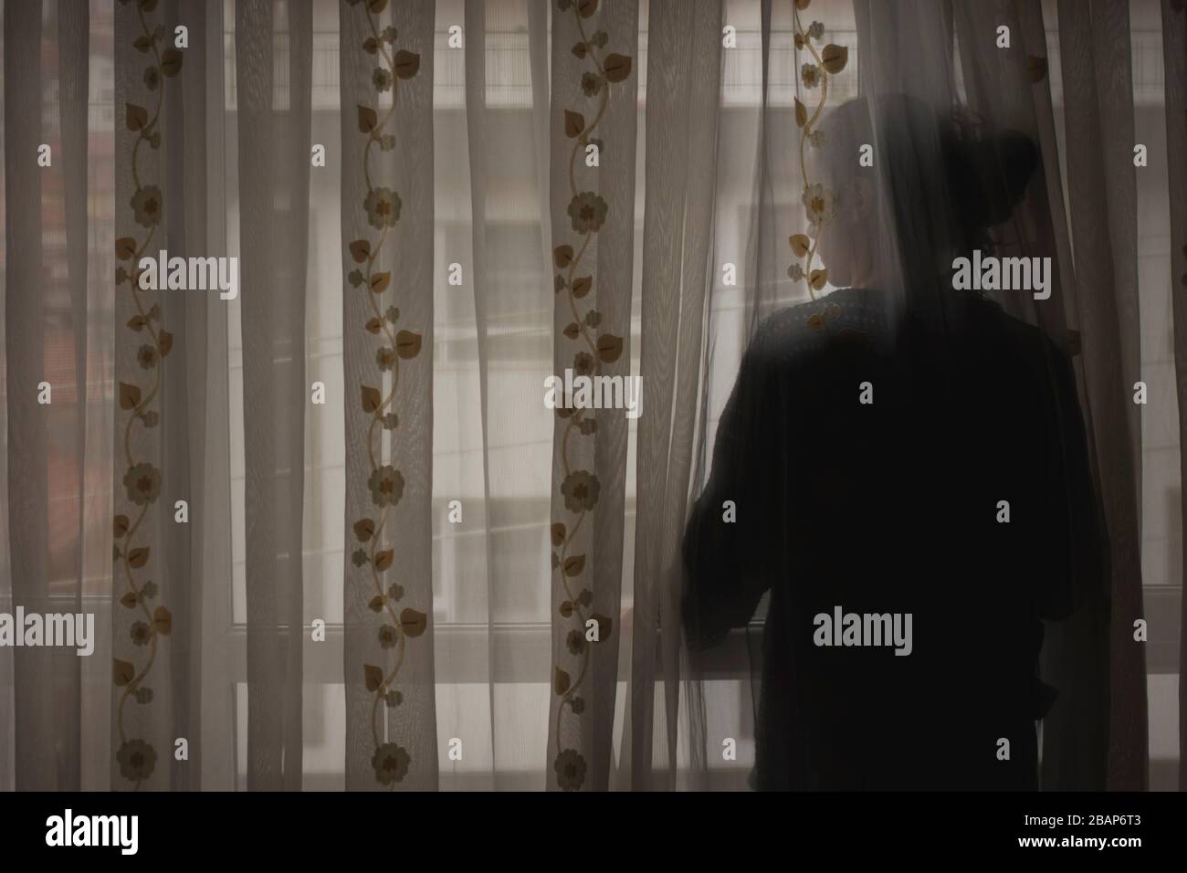 Teen in front of curtain watching the empty street from his window ...