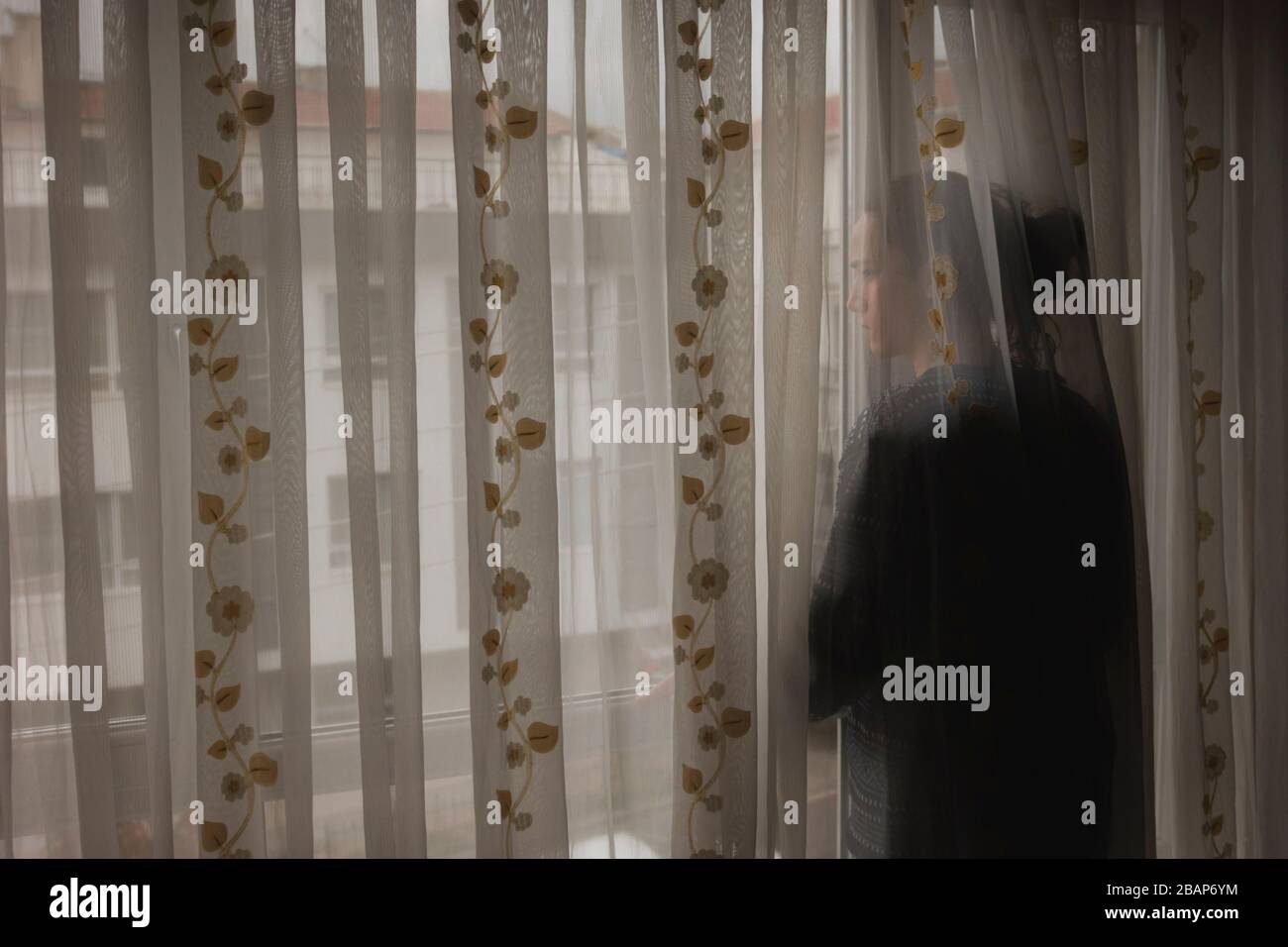 Teen in front of curtain watching the empty street from his window ...