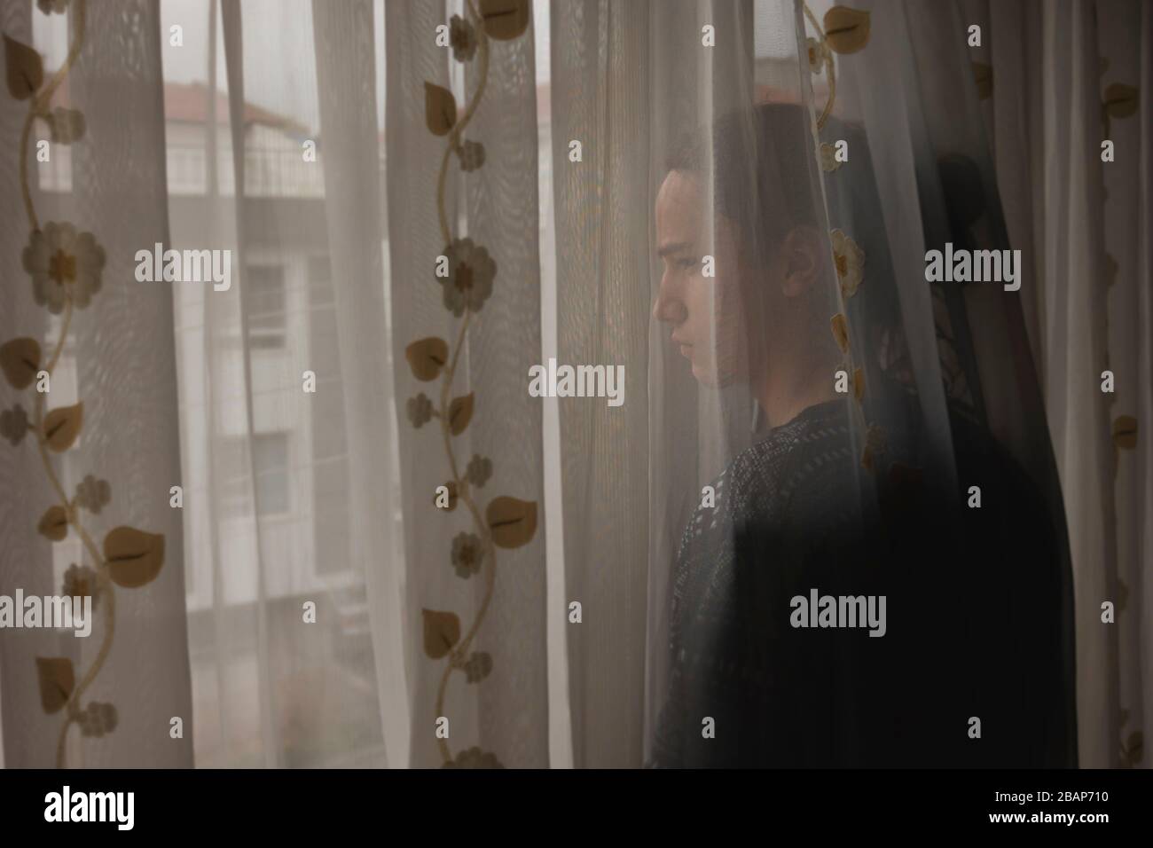 Teen in front of curtain watching the empty street from his window in ...