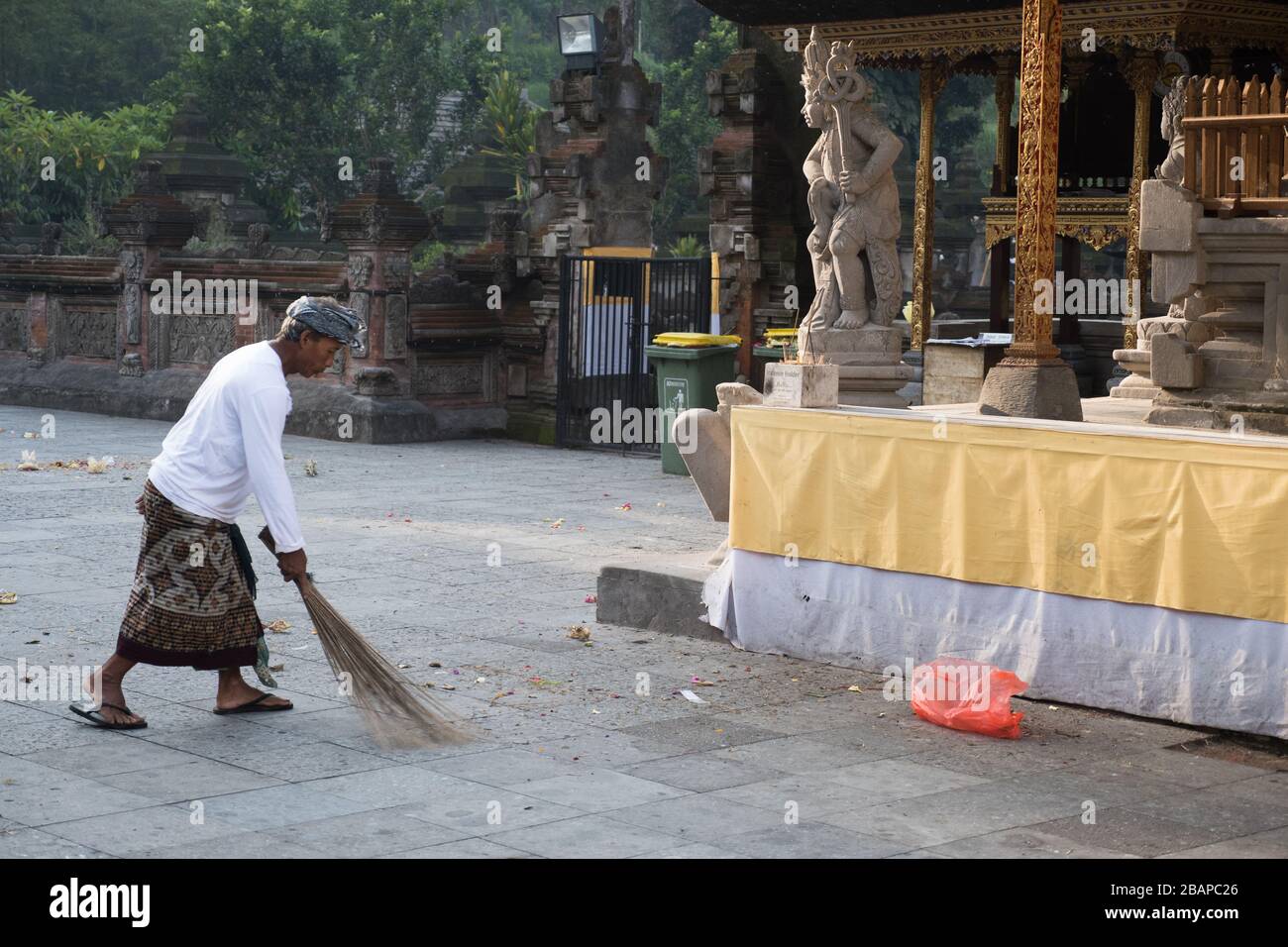 Temple employee dressed in traditional Balinese clothing sweeping inner ...