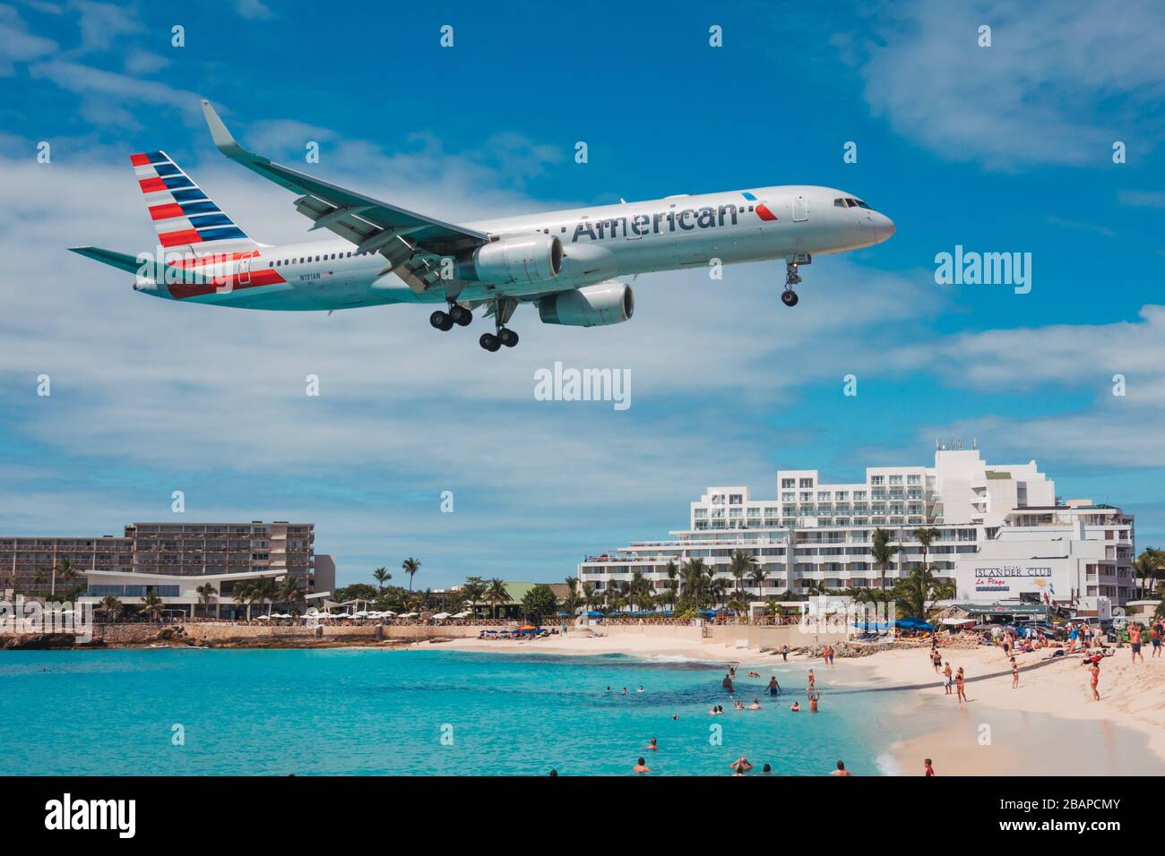 An American Airlines Boeing 757 flies over tourists sunbathing and ...