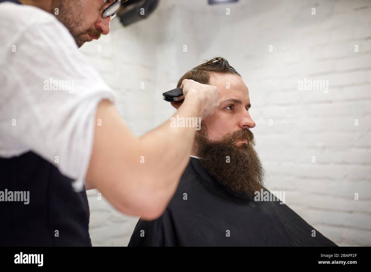 Master cuts hair and beard of men in the barbershop, hairdresser makes ...