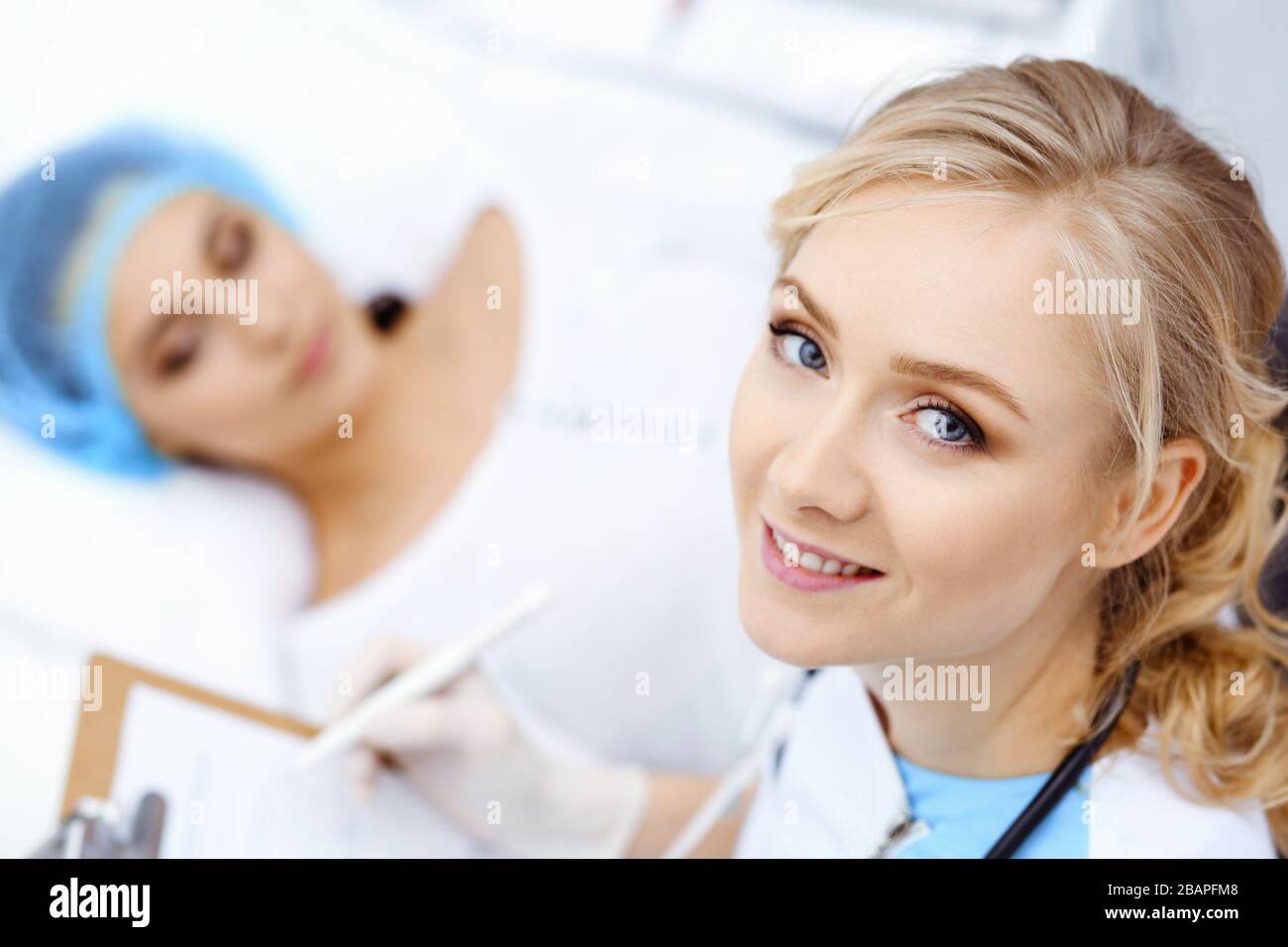 Female doctor and young woman patient in hospital. Physicians examine girl lying at the bed ...