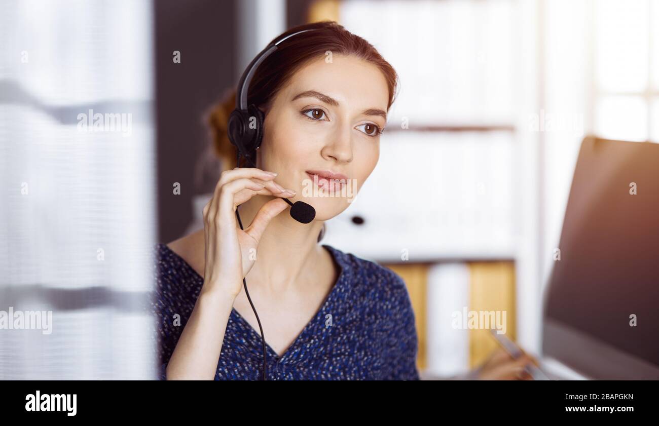 Latin american businesswoman talking by headset in sunny office. Call ...