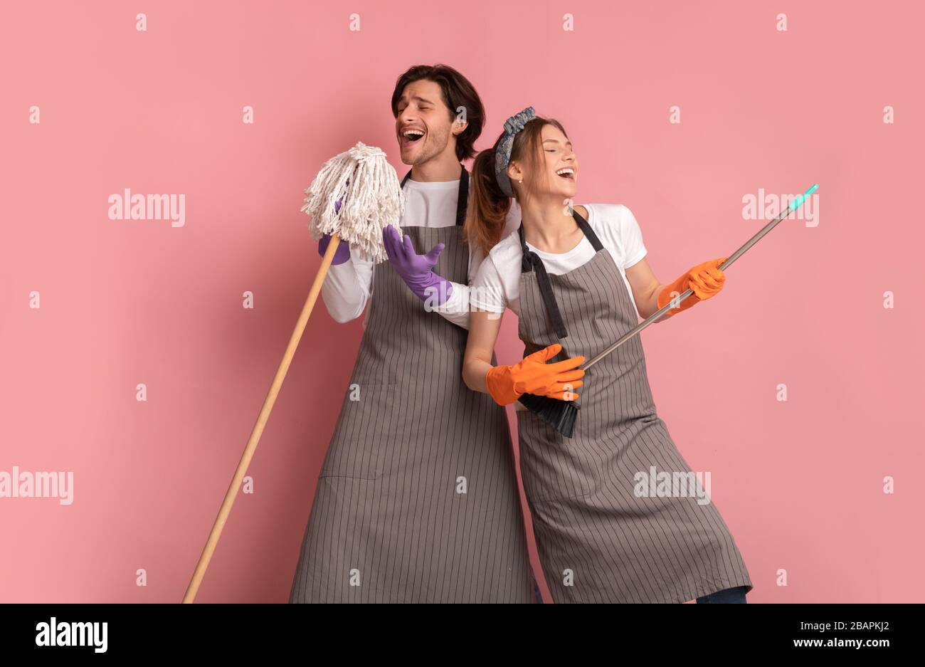 Millennial couple having fun during spring cleaning, using broom like ...
