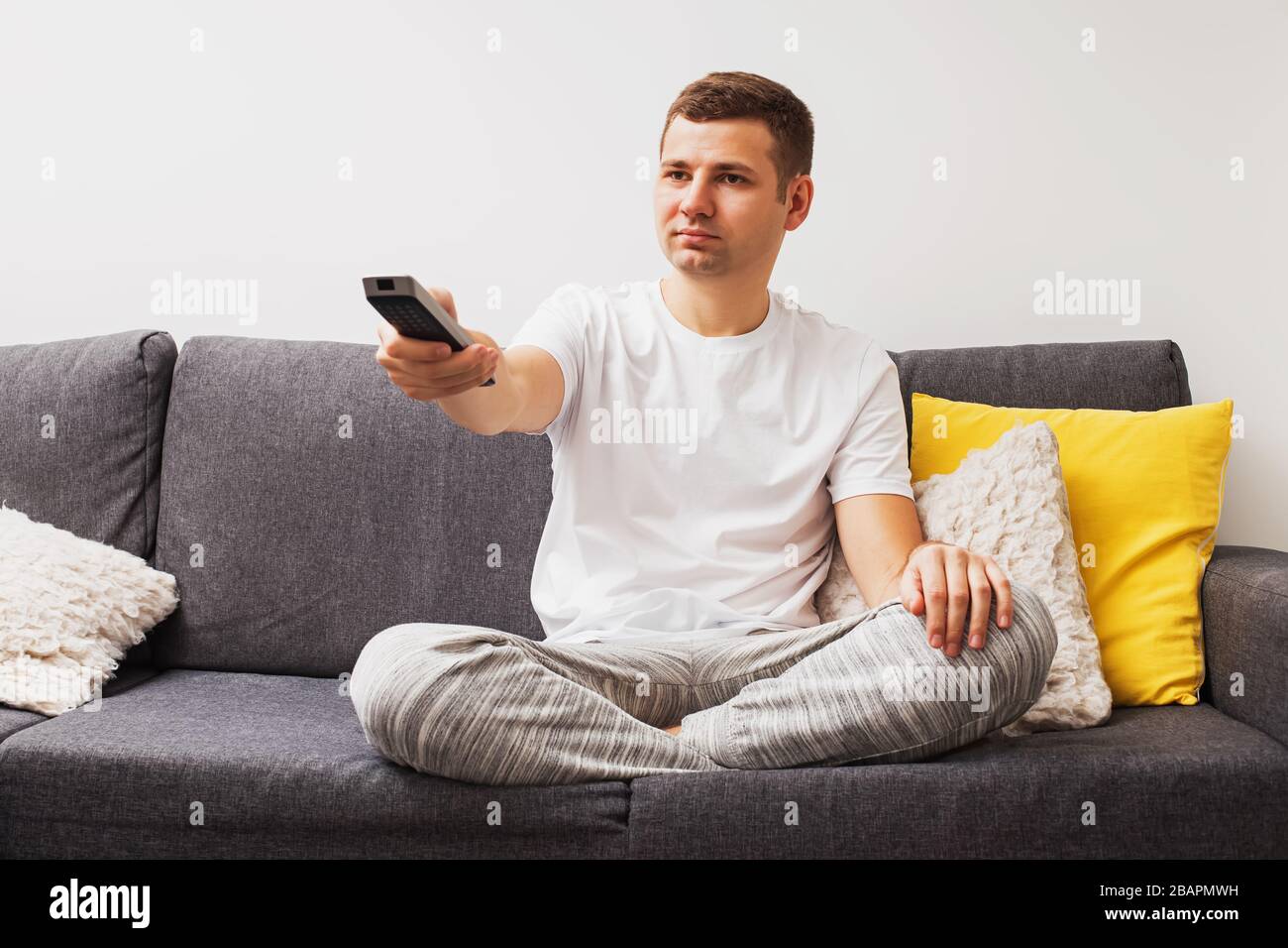 Young man sitting on sofa and holding tv remote control Stock Photo - Alamy