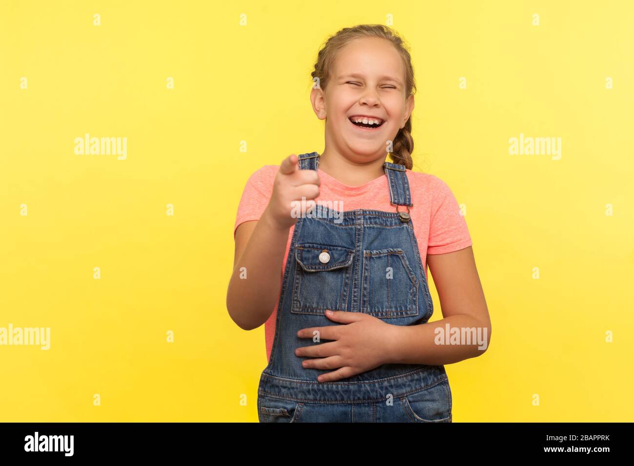 Hey you! Portrait of glad little girl with braid in denim overalls ...
