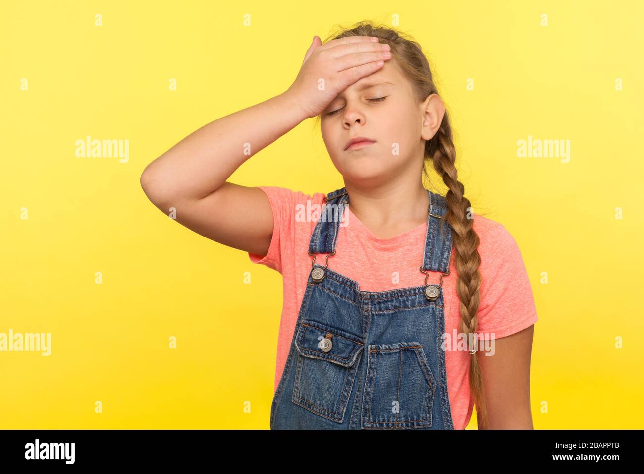 Portrait of forgetful sad little girl with braid in denim overalls ...