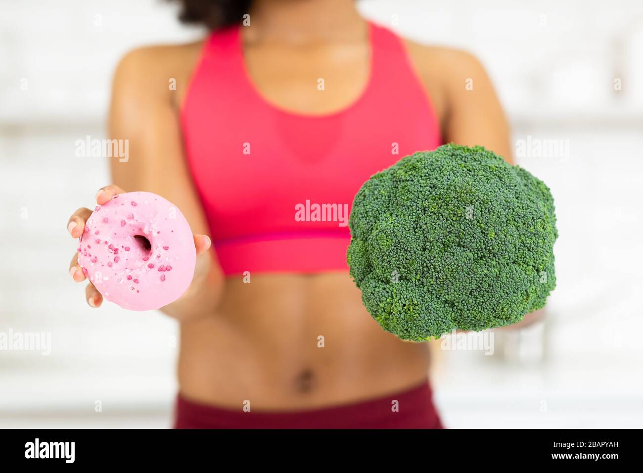 Fit Afro Girl Holding Broccoli And Doughnut Stock Photo - Alamy