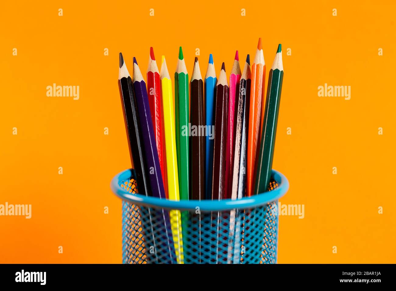blue metal bucket with colored pencils for office on an orange ...