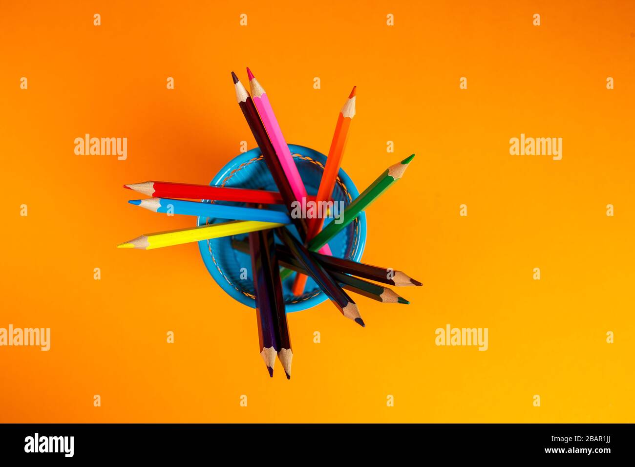 blue metal bucket with colored pencils for office on an orange ...