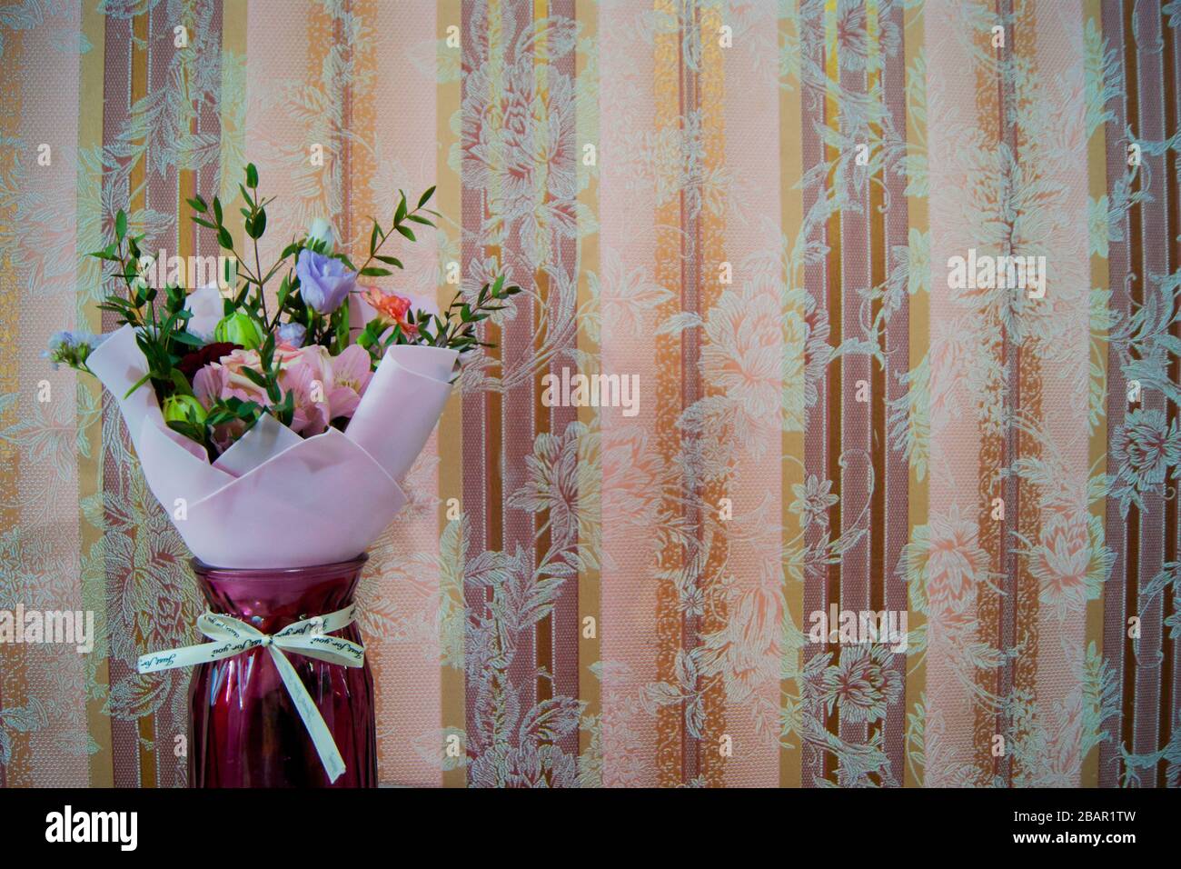 A delicate bouquet of different flowers in a light pink wrapper stands ...