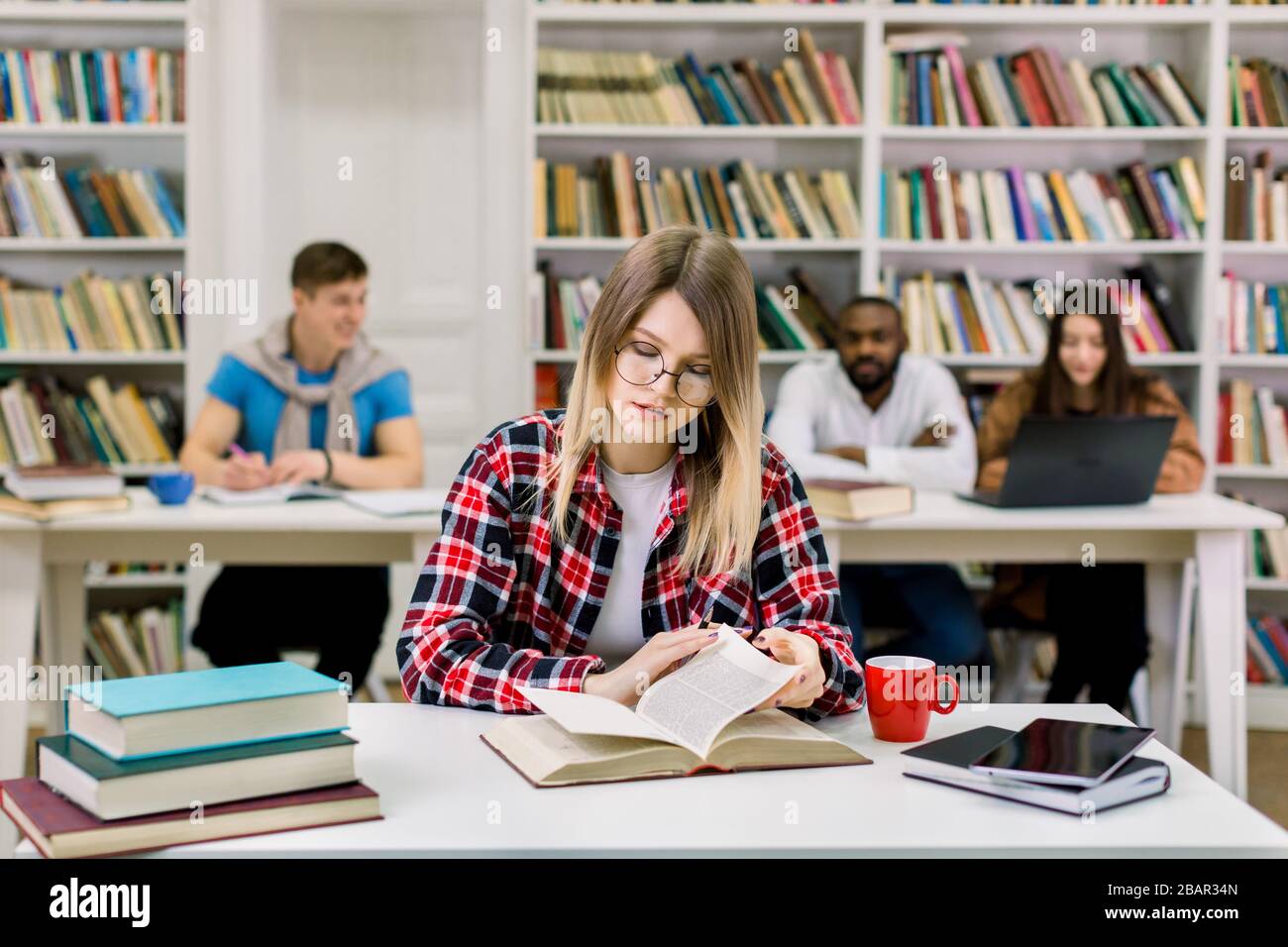 Portrait of a pretty young student girl studying at college library ...