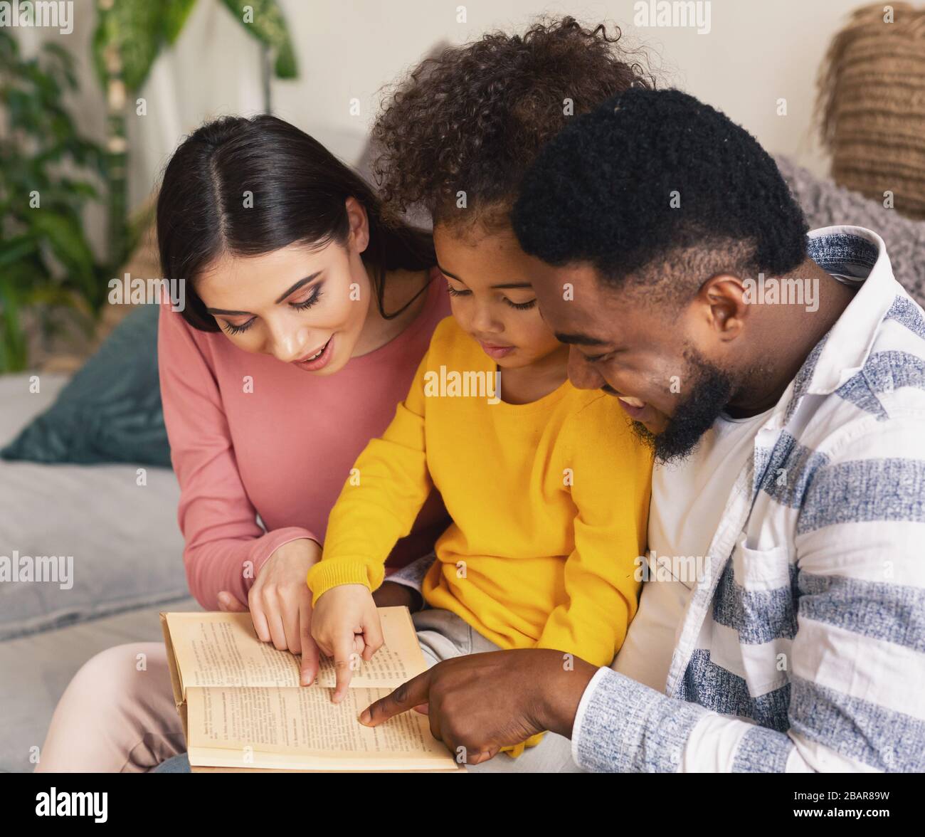 Parents helping daughter read book at home Stock Photo - Alamy