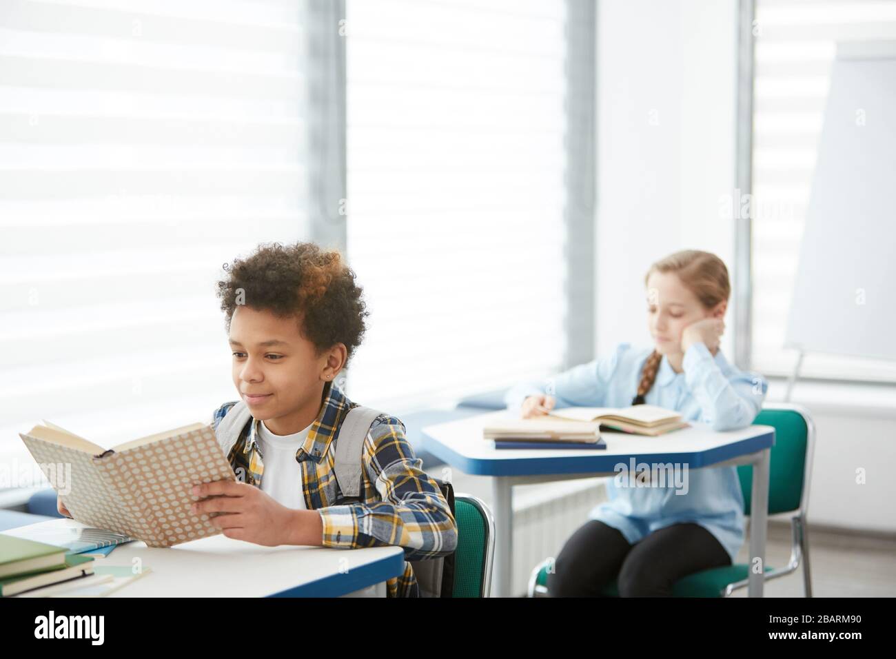 Portrait of two kids sitting at desks in modern school classroom, focus ...