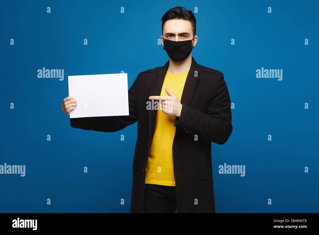 Young handsome man holding blank sheet of paper, isolated at the blue ...