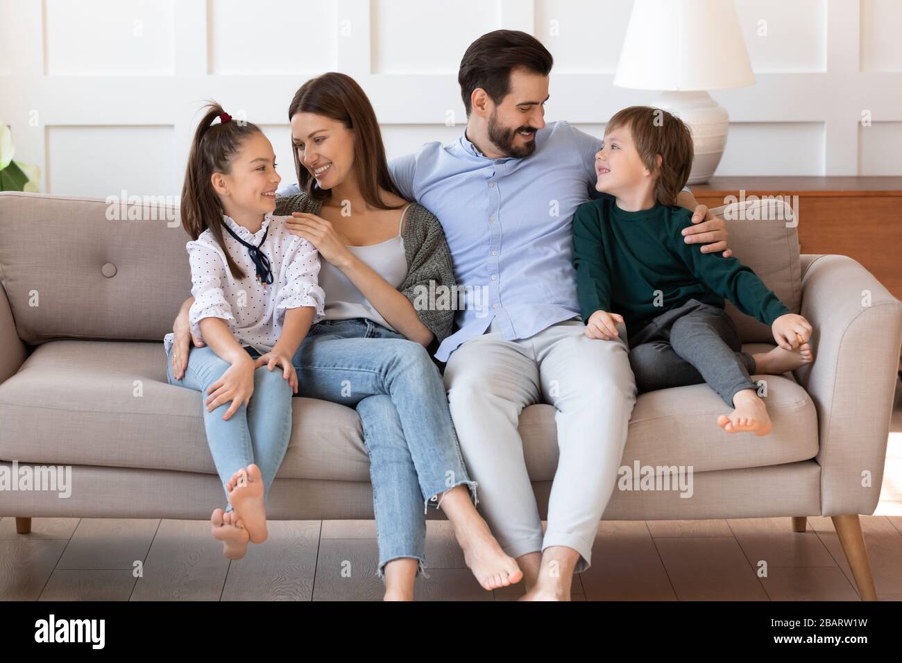 Affectionate young parents relaxing on sofa, cuddling small children ...