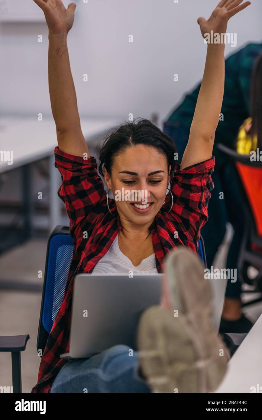 A young female worker with her hands up in the air, her legs on the ...