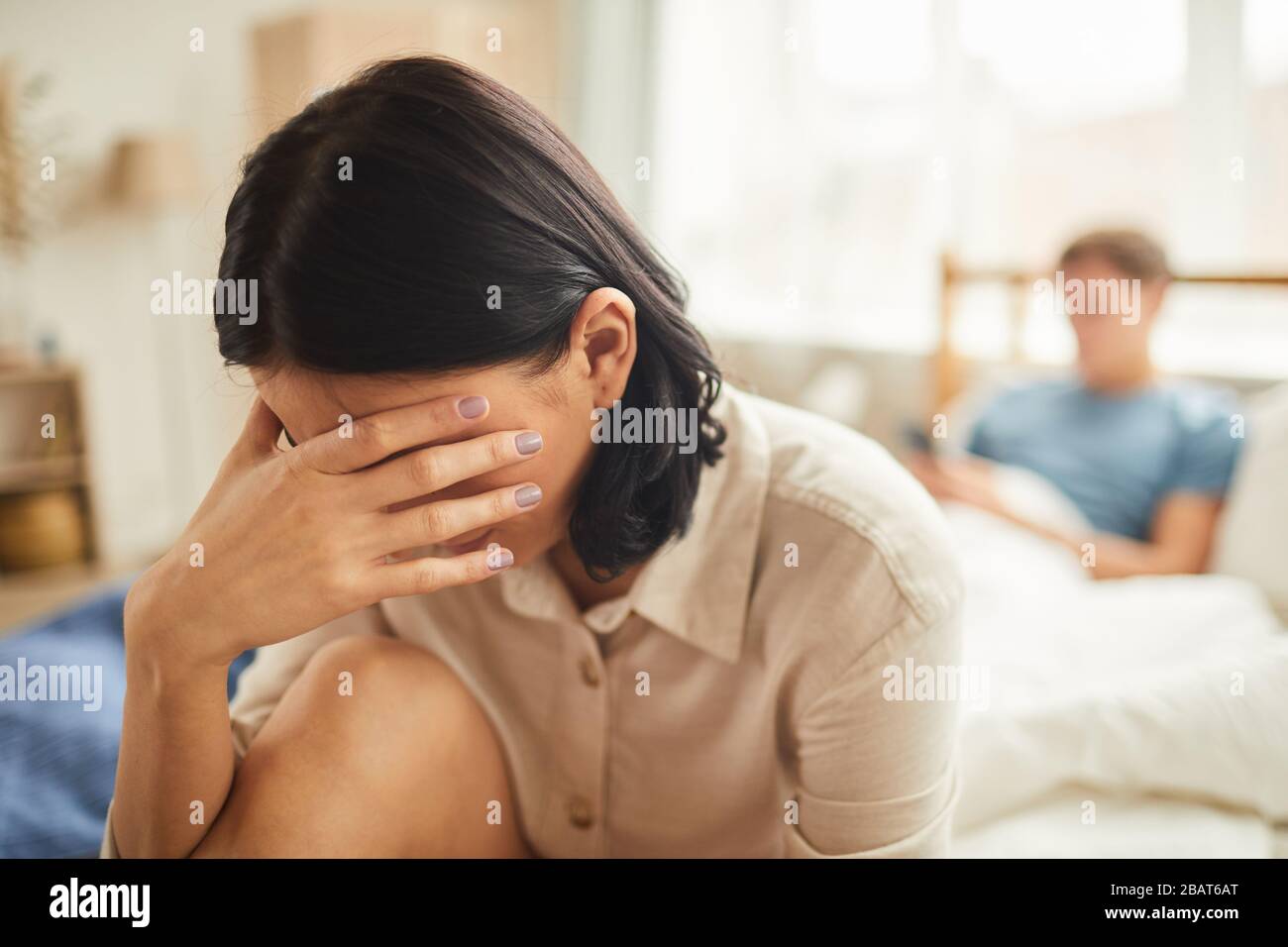 Portrait of frustrated young woman crying in bedroom with husband in ...